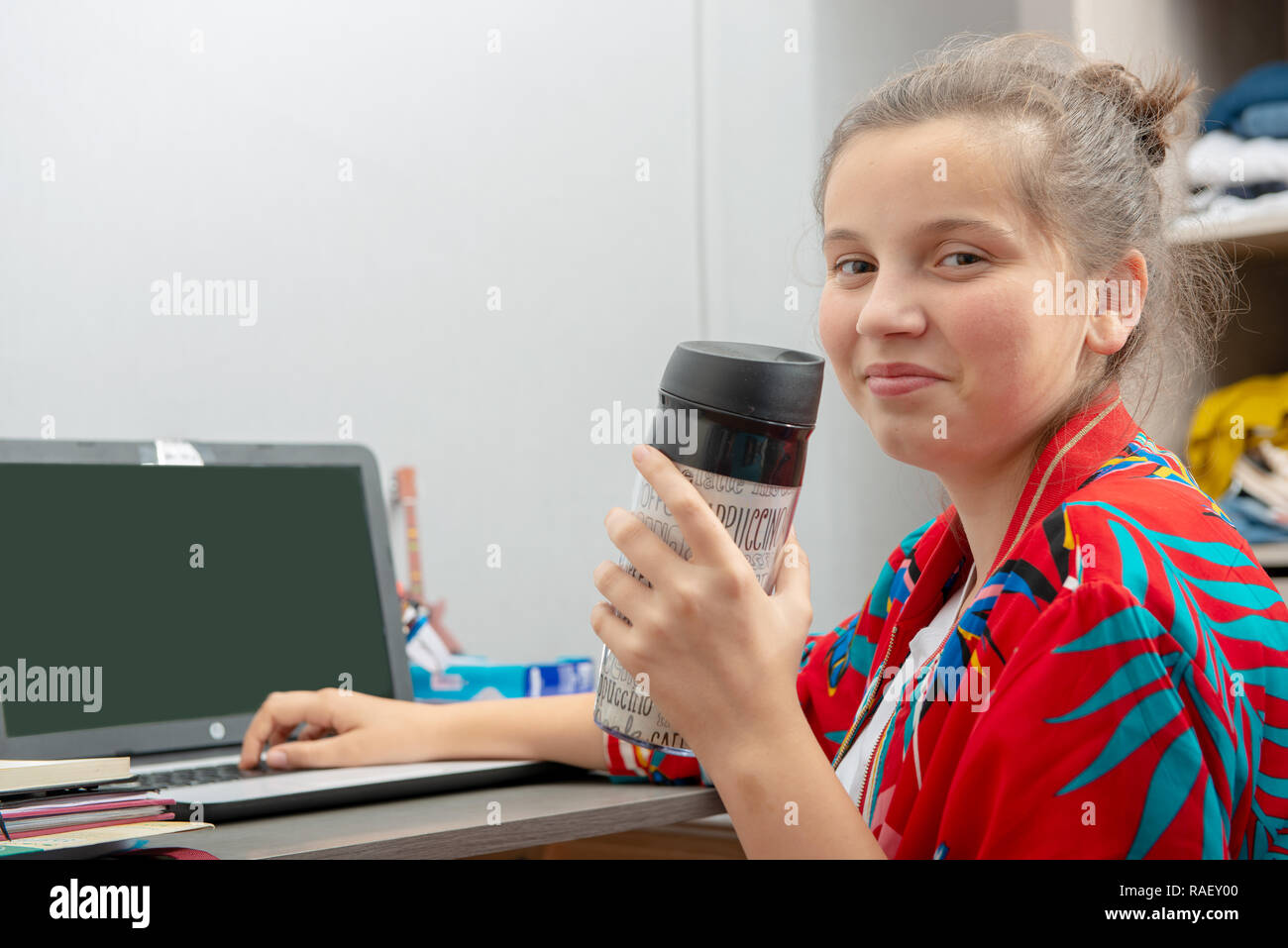 a pretty teenage girl doing homework on the desk and drinking Stock ...