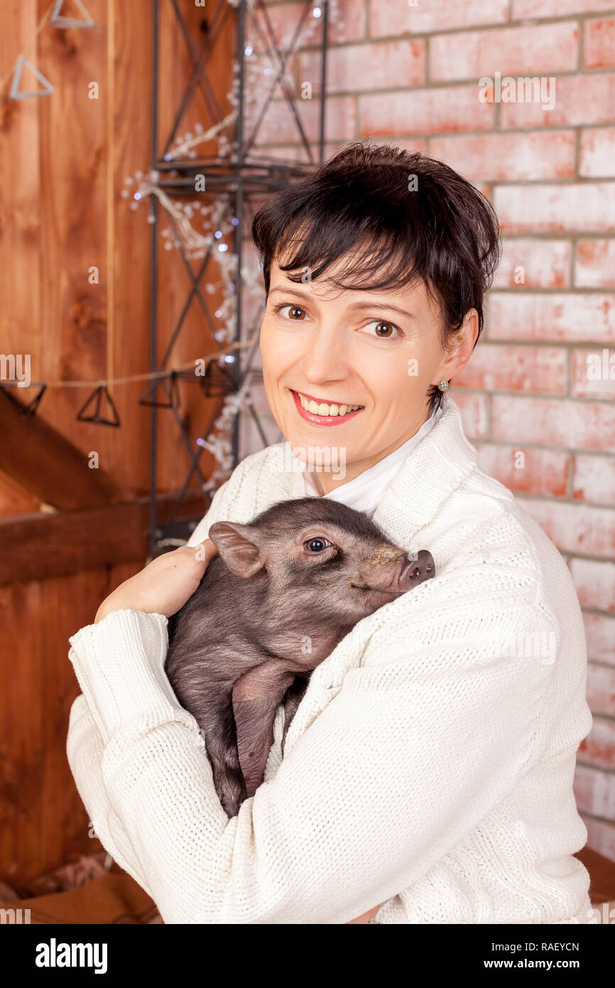 A baby mini-pig and beautiful woman near Christmas Tree, symbolizing ...