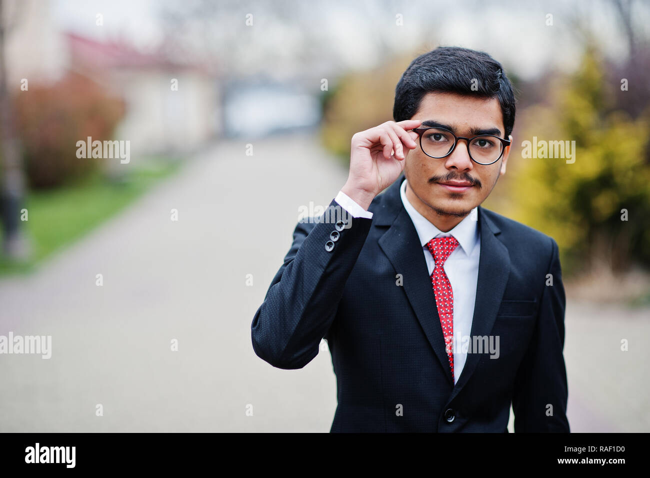 Indian young man at glasses, wear on black suit with red tie posed ...