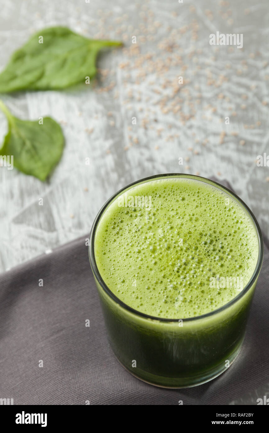 Fresh green spinach smoothie in a glass cup on a gray wooden surface ...