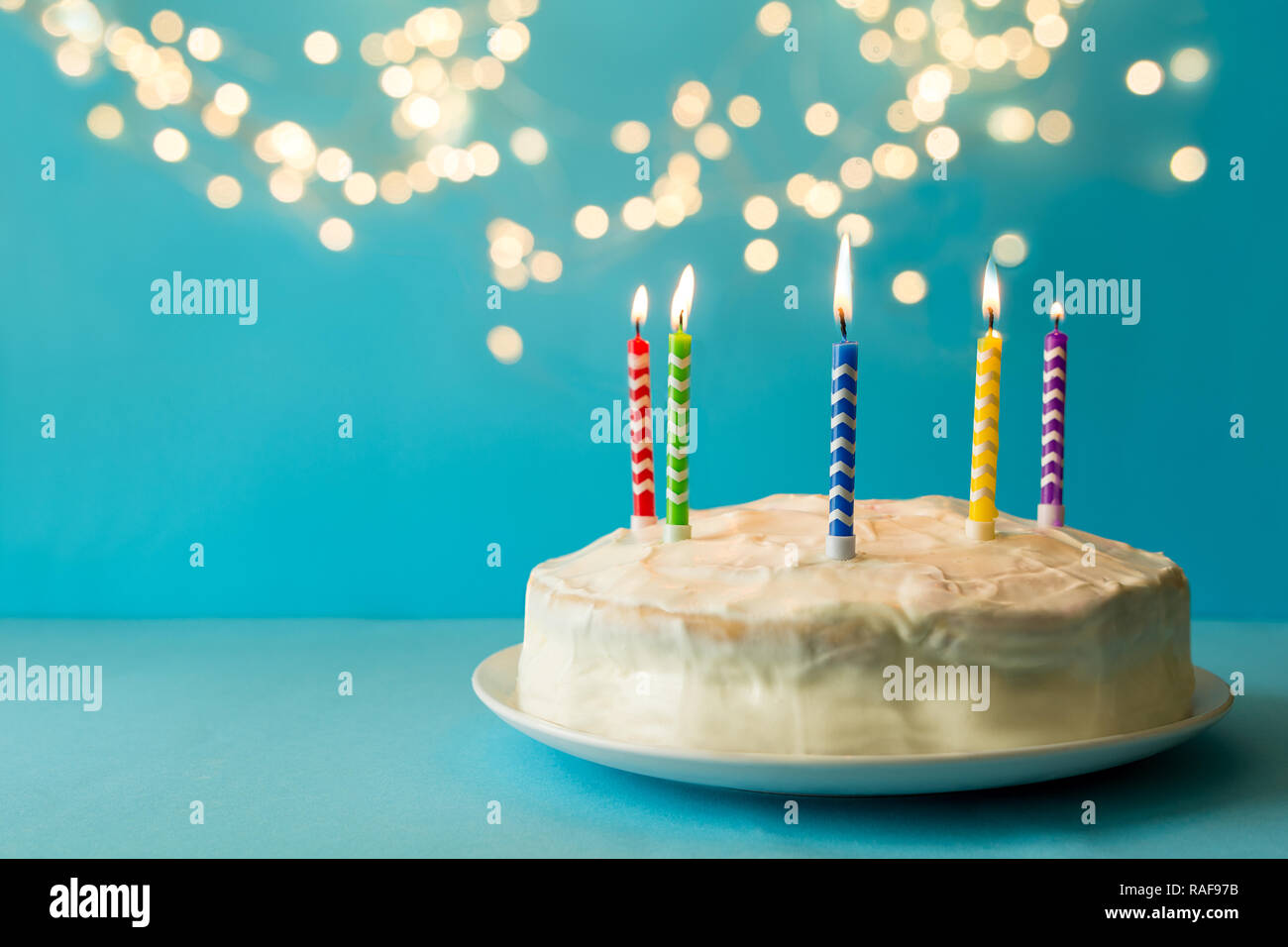 White birthday cake with colorful candles on blue background against ...
