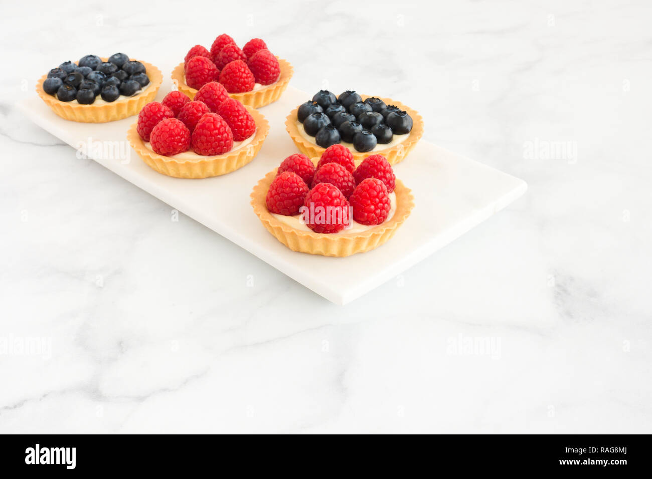Homemade blueberry and raspberry and tarts on white marble board and ...