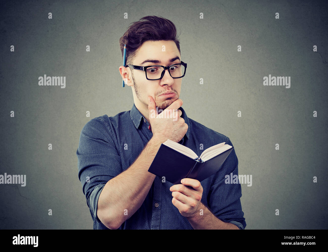 Young smart man in glasses reading book with interesting notes while ...