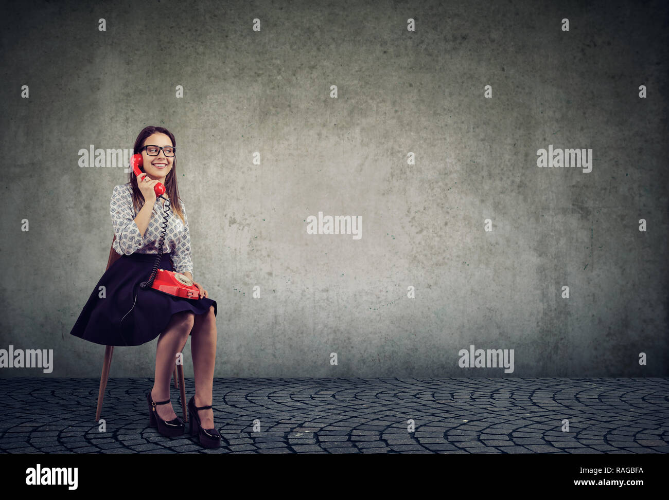 Young woman sitting on chair and having telephone call against gray ...