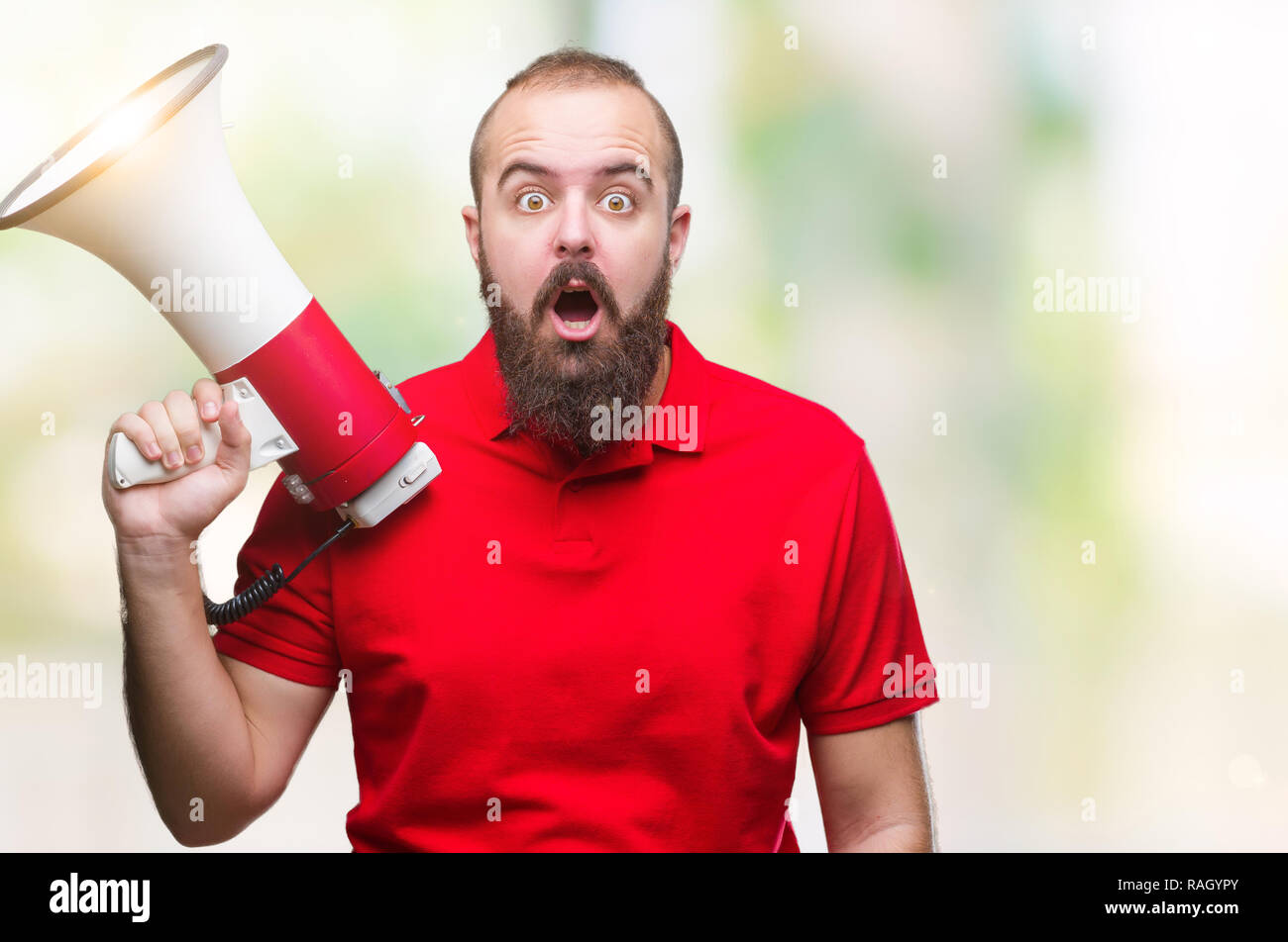 Young caucasian man shouting through megaphone over isolated background ...