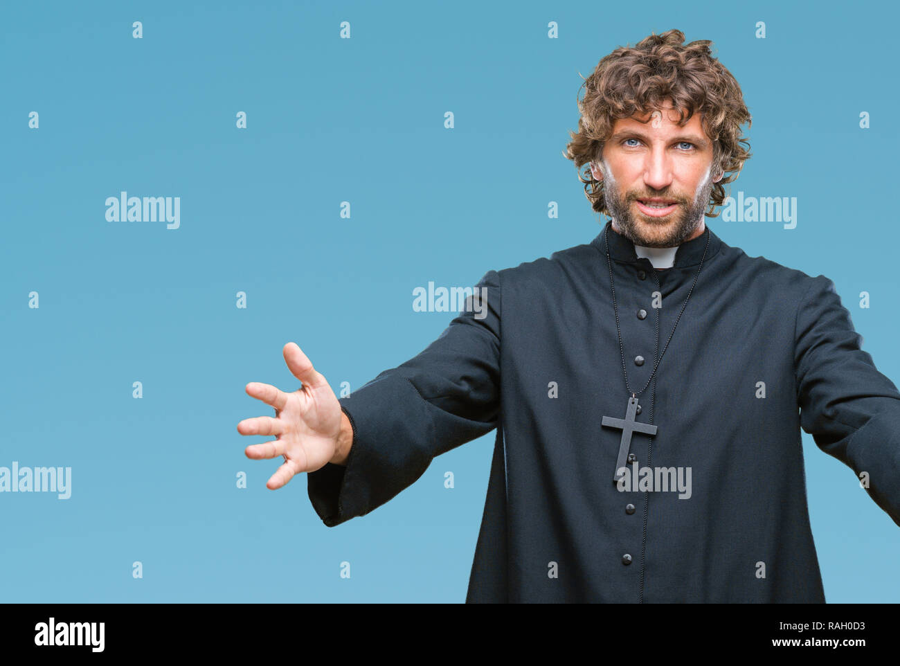 Handsome hispanic catholic priest man over isolated background looking ...