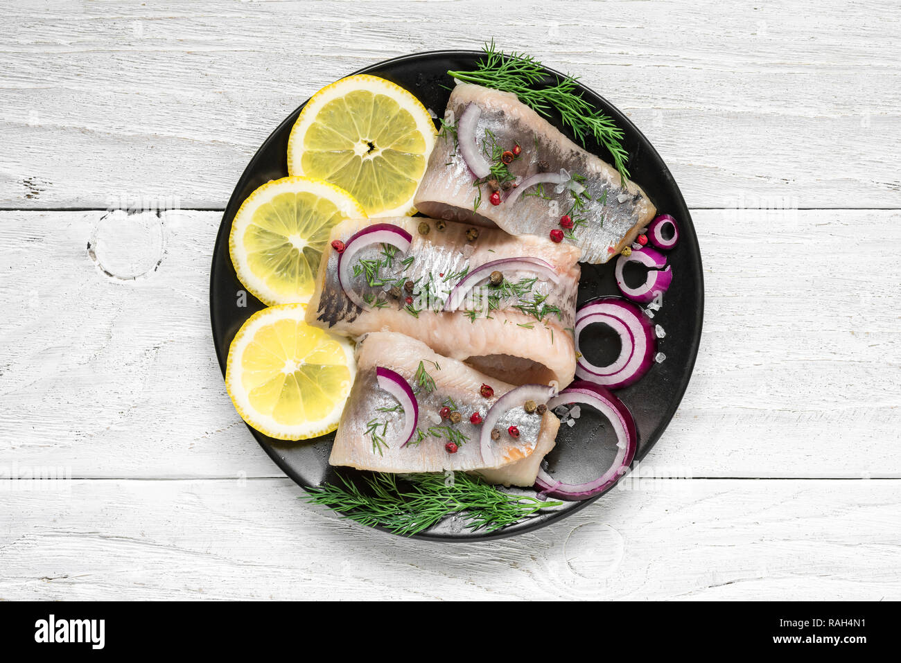 Herring fillet with salt, pepper, herbs, onion and lemon on black plate ...