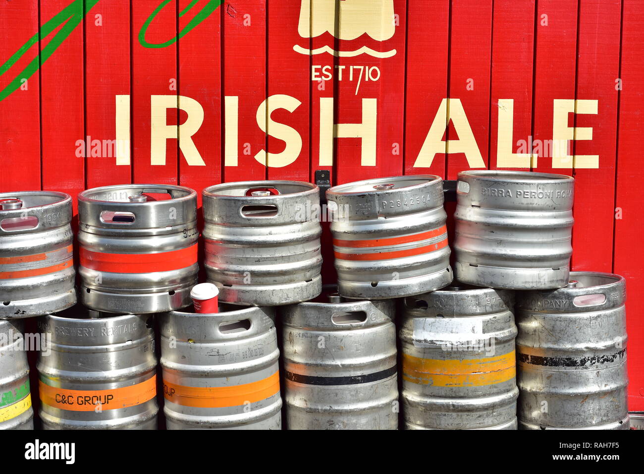 Metal beer barrels stacked in front of red wooden wall advertising ...