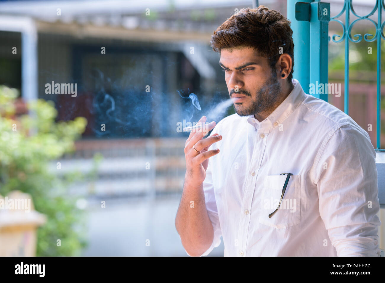 Young stressed bearded Indian man thinking while smoking outdoors Stock ...