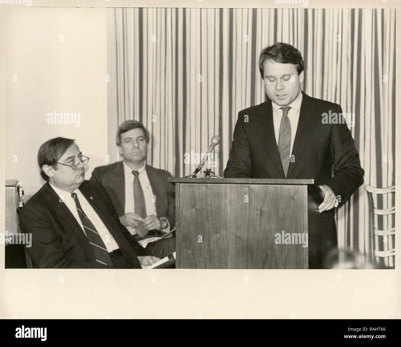 MAN AT THE PODIUM TALKING TO A GROUP OF PEOPLE WITH TWO MEN SITTING ...