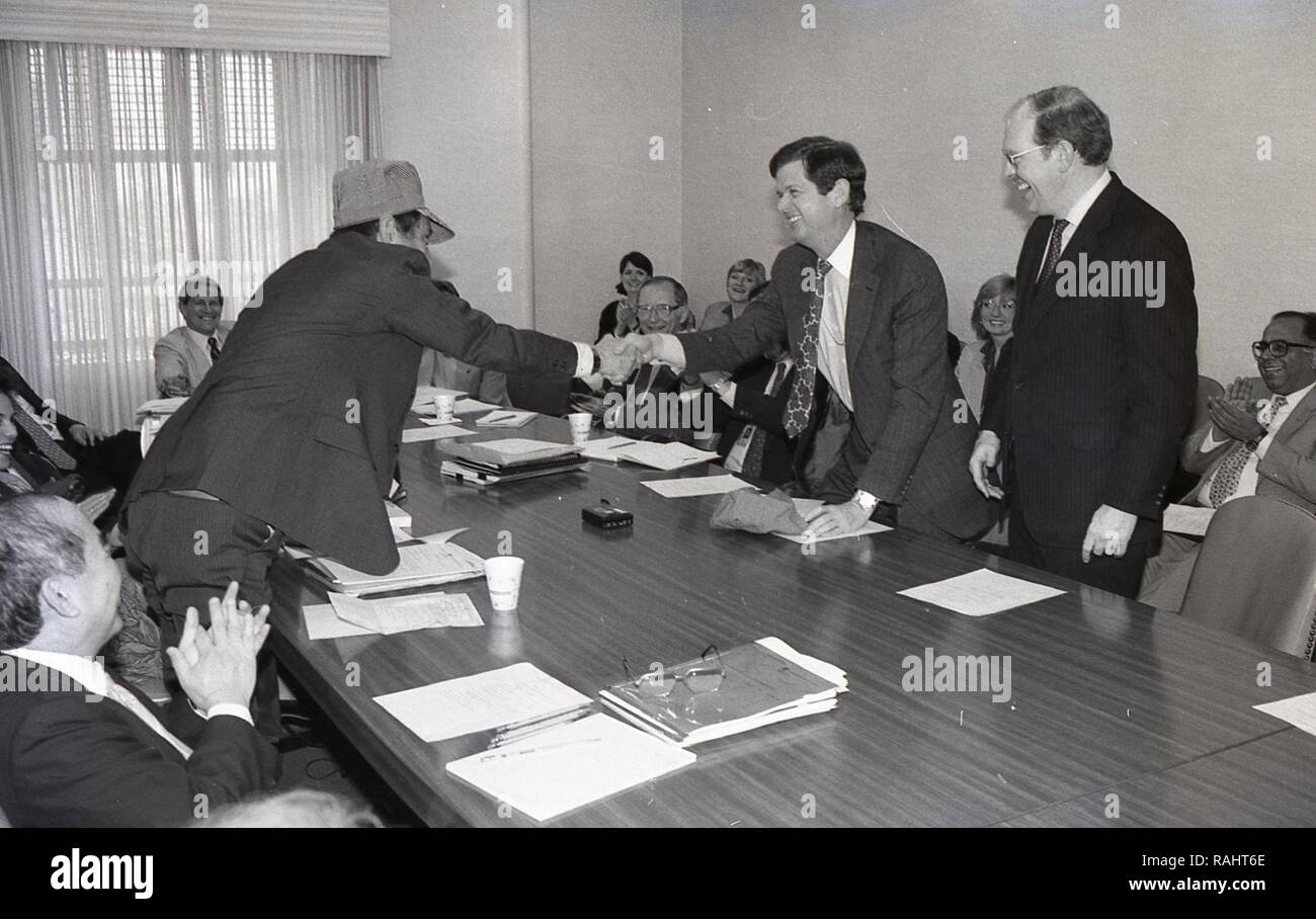 TWO MEN GREETING EACH OTHER ACROSS THE TABLE WITH OTHER MEN AND WOMEN ...