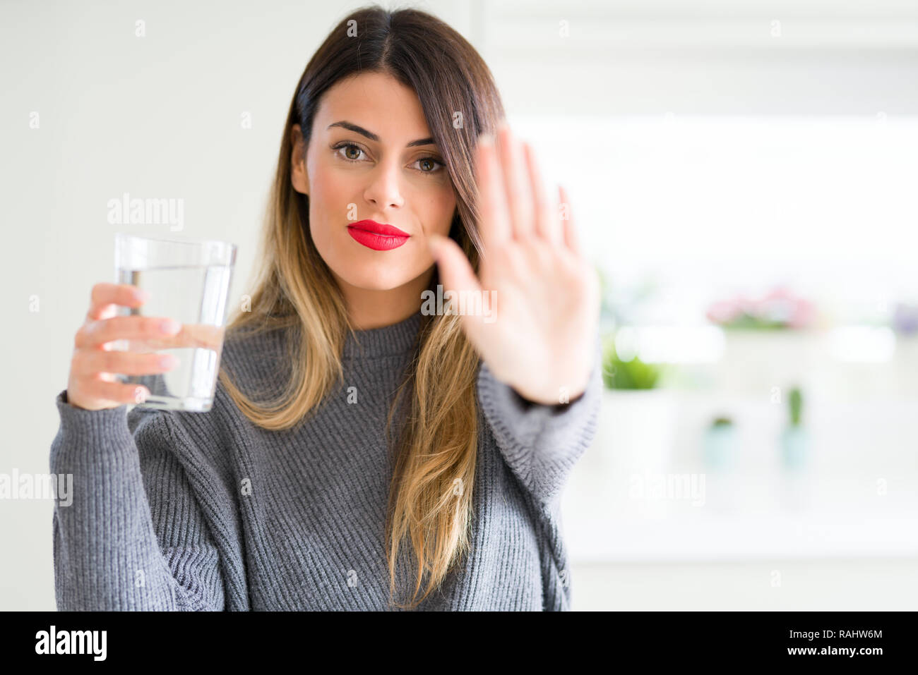 Young beautiful woman drinking glass of water at home with open hand ...