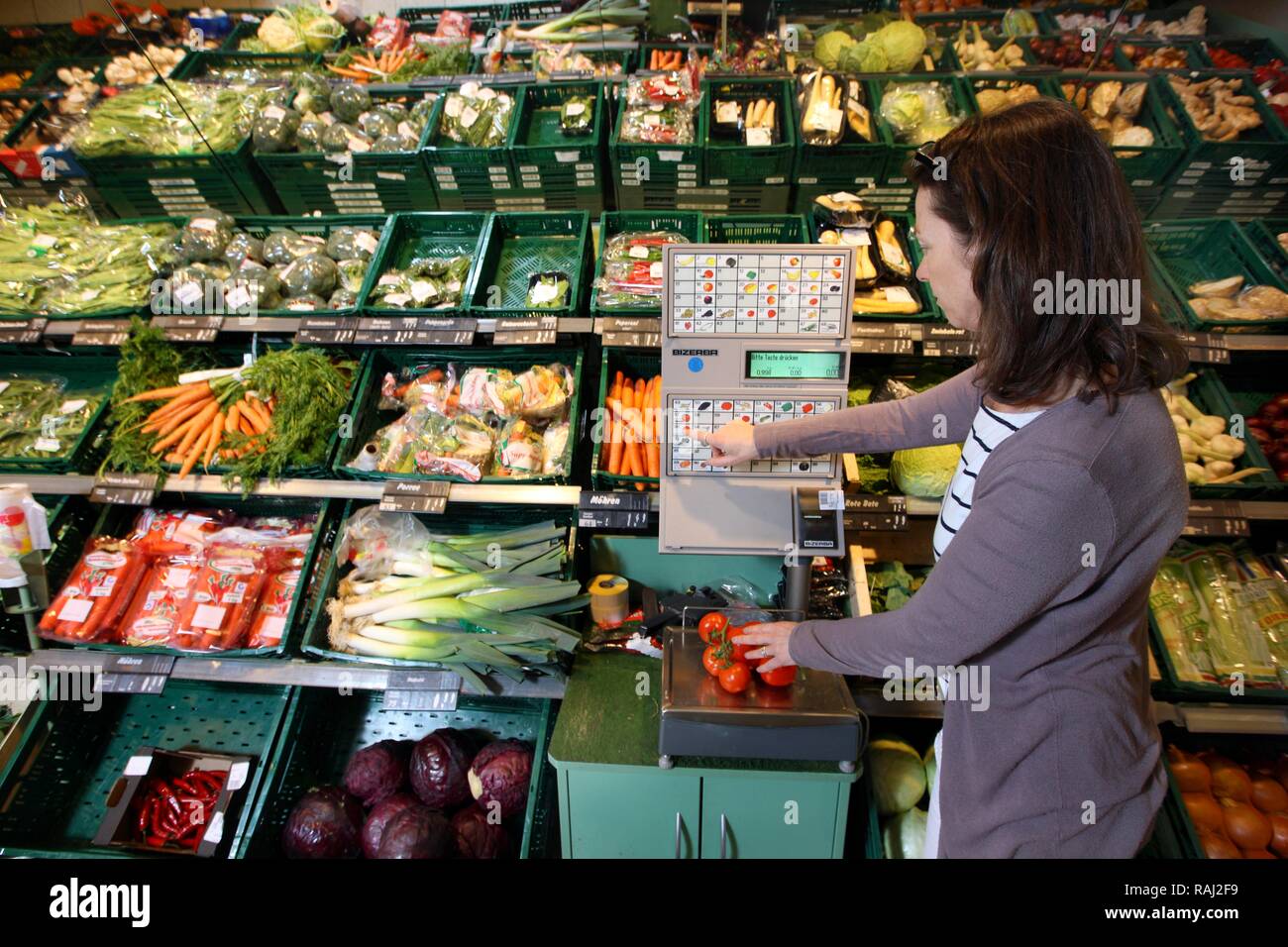Woman weighing vegetables in the fruit and vegetable section of a self-service grocery ...