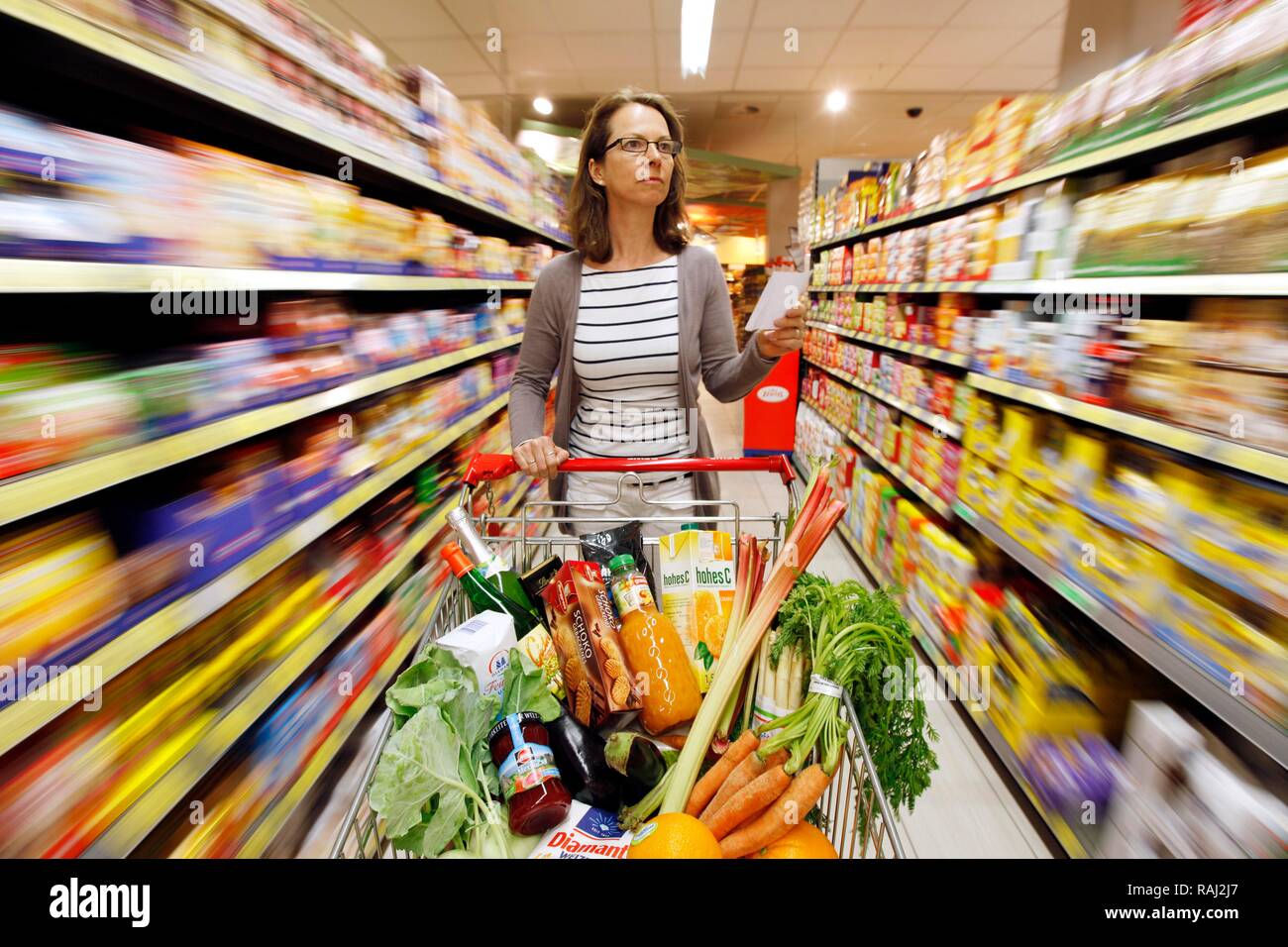 Woman pushing a full shopping cart through a corridor of the food ...