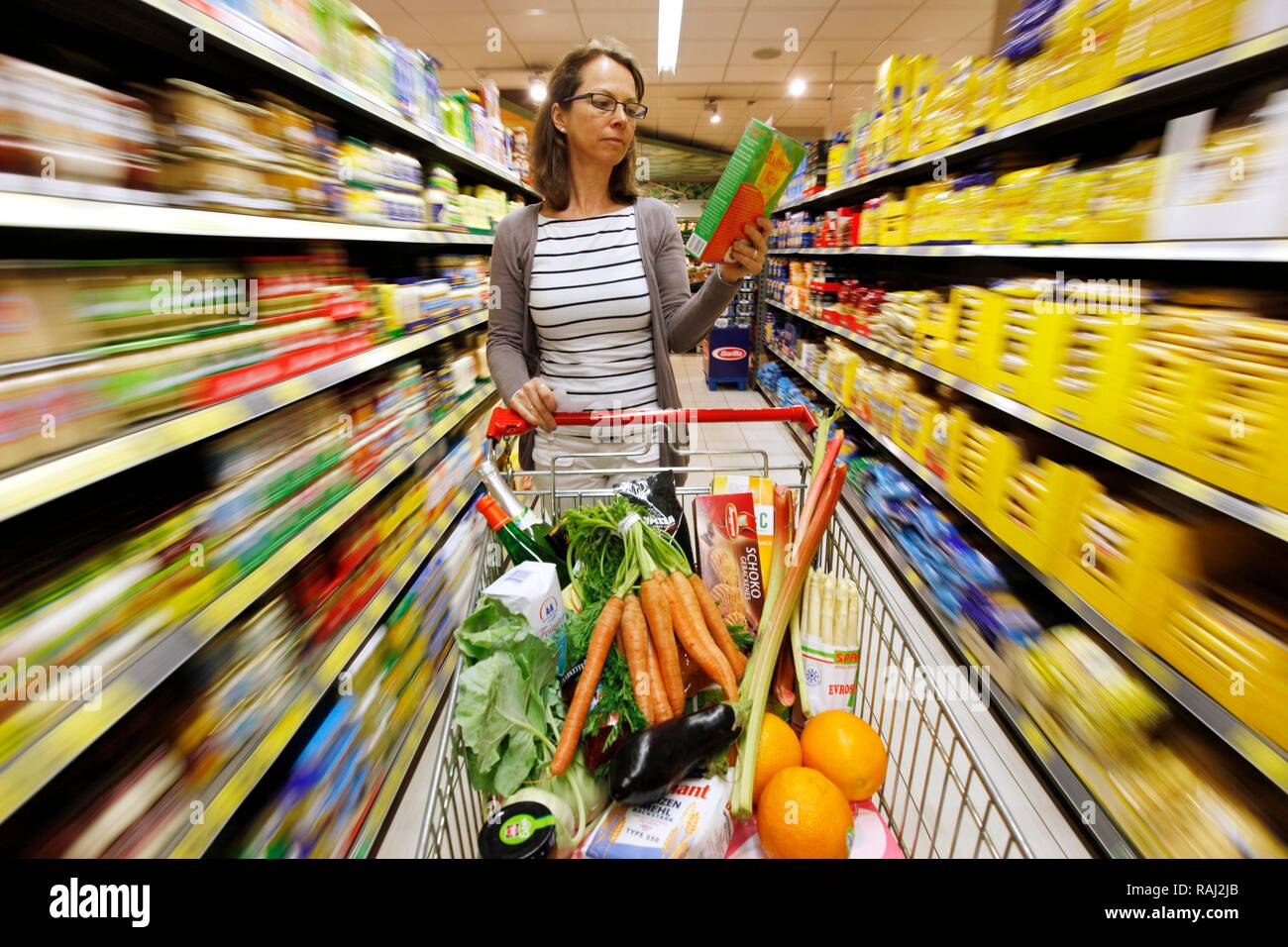 Woman pushing a full shopping cart through a corridor of the food ...