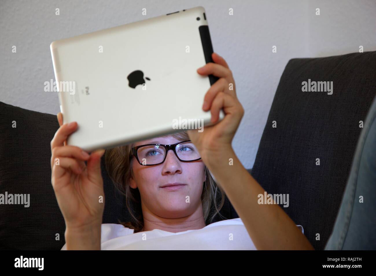 Young woman lying on a sofa and surfing with an iPad, tablet computer ...
