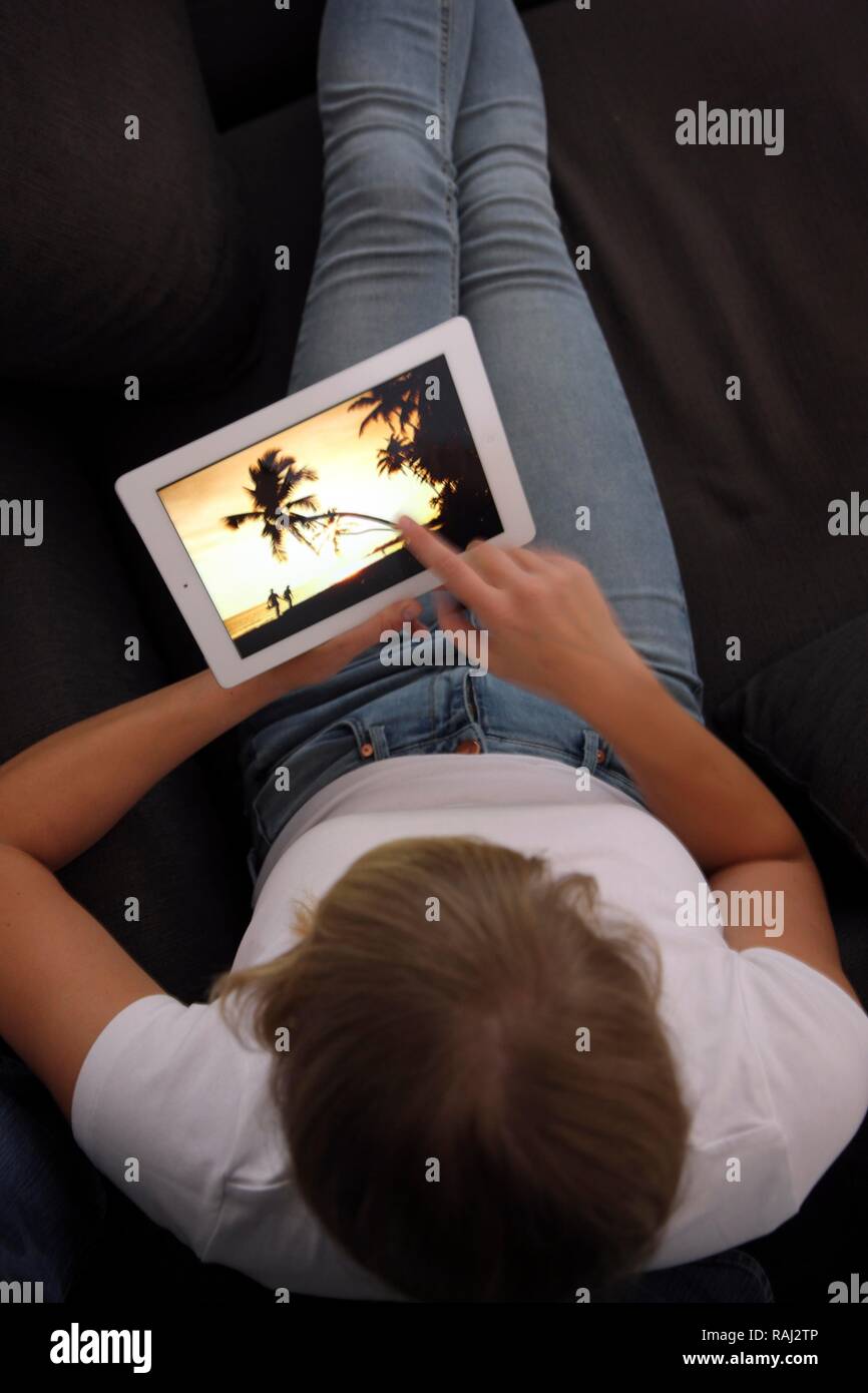 Young woman sitting on a sofa and surfing with an iPad, tablet computer ...