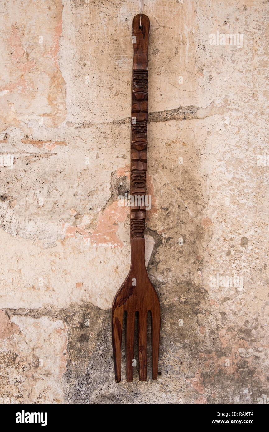 Giant dark brown fork hanged in front of a restaurant with light stone ...