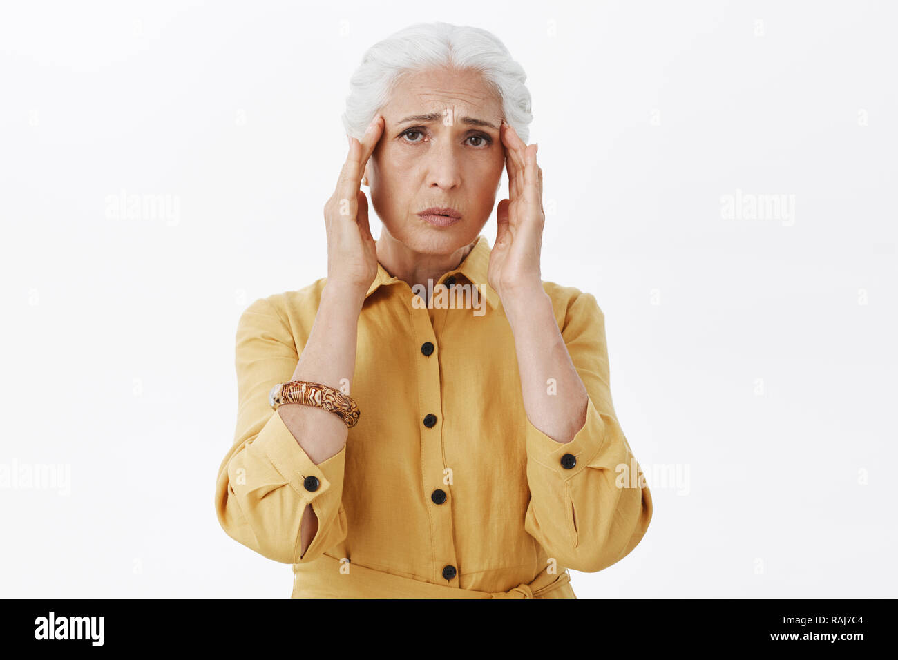 Studio shot of gloomy drained and upset old woman in trendy yellow coat ...