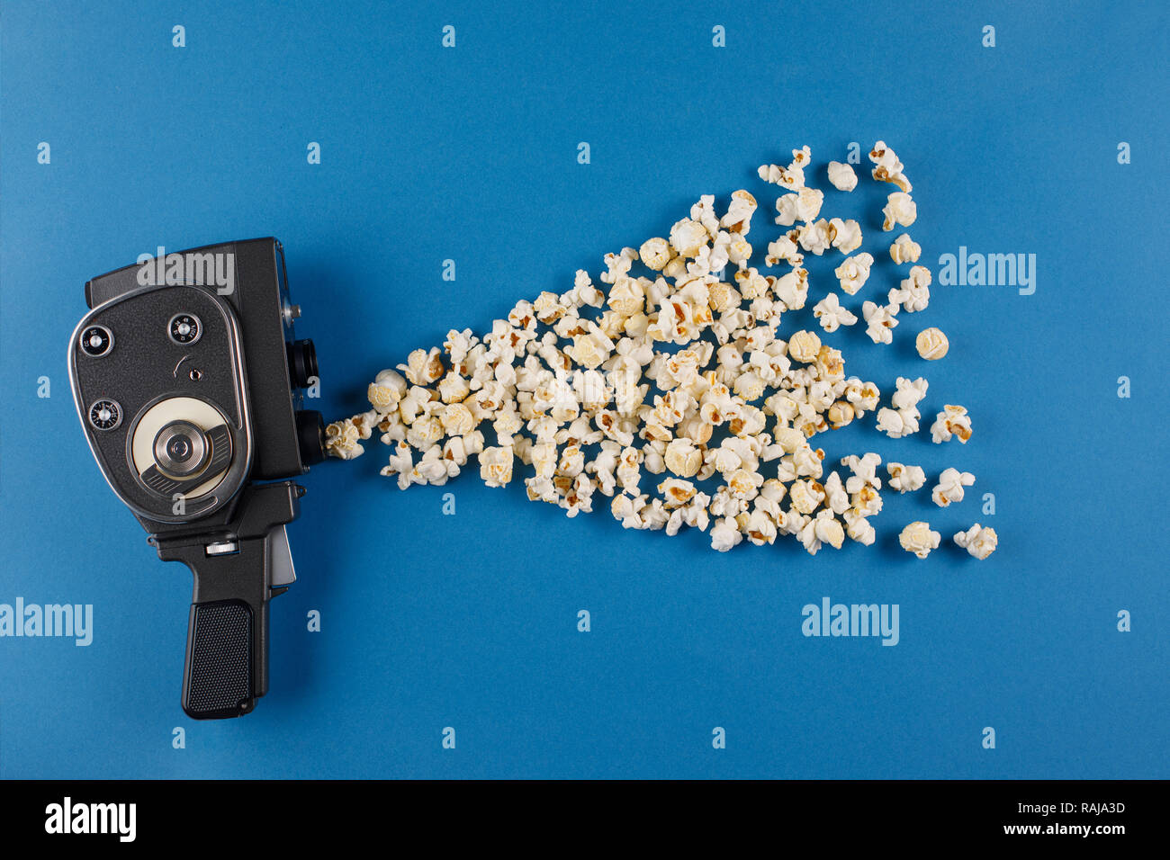 Retro movie camera with popcorn flying out of it on a blue background ...