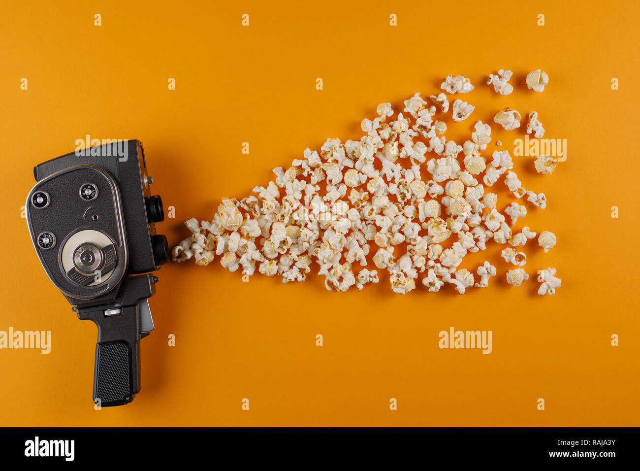 Retro movie camera with popcorn flying out of it on a yellow background ...