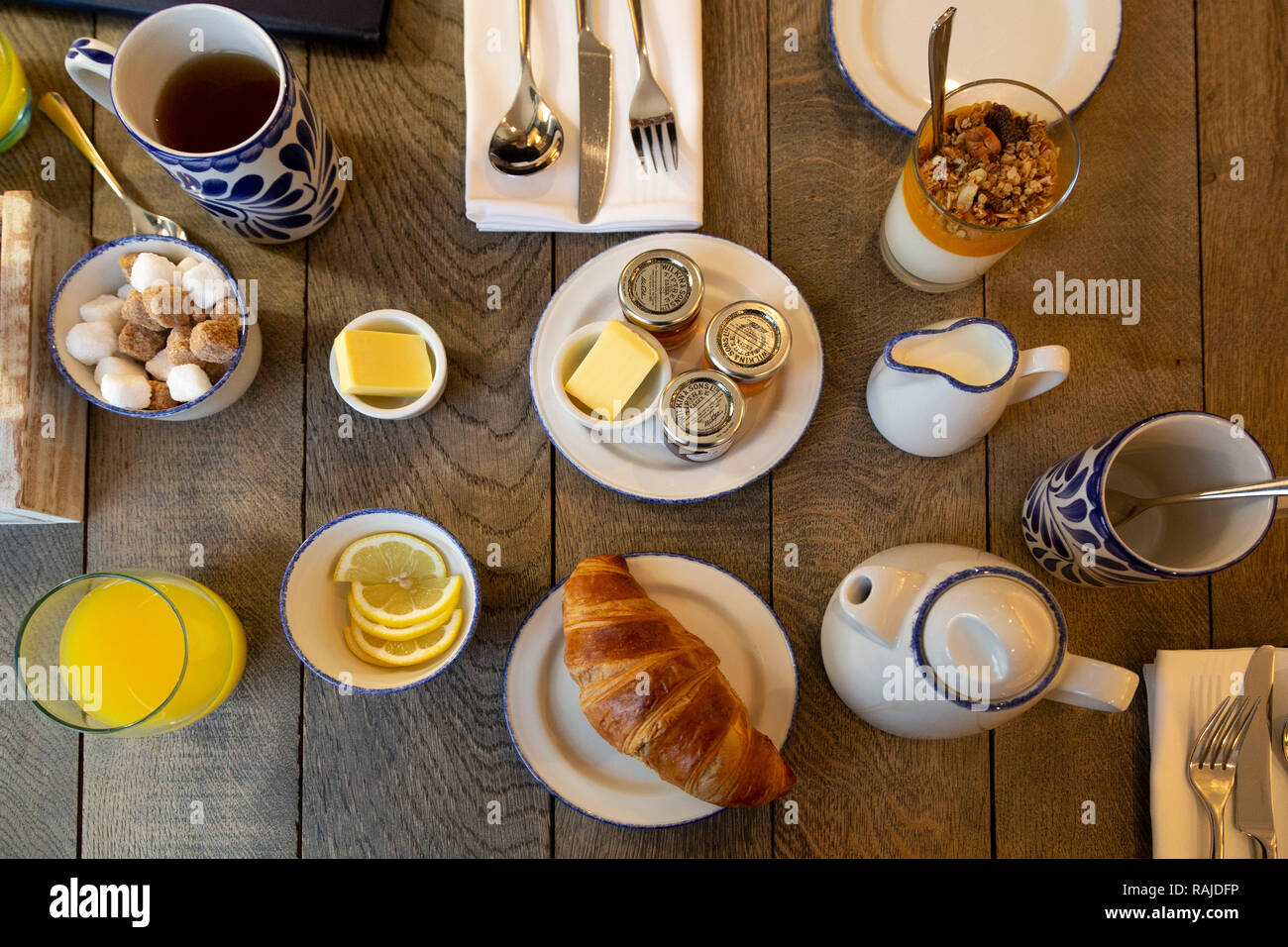 A breakfast table with a croissant, preserves and orange juice. Teacups ...