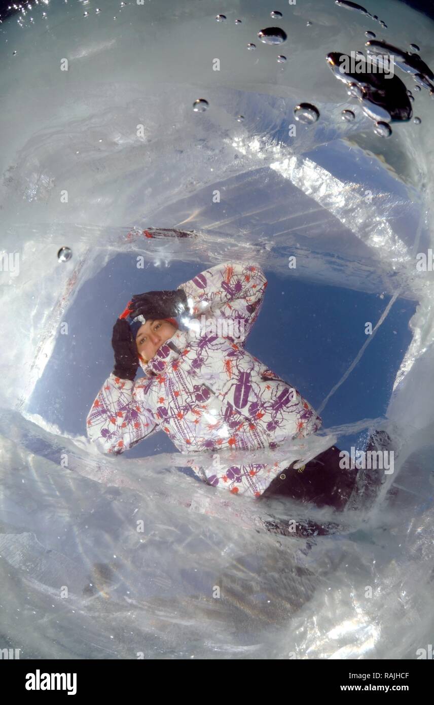 Girl looking through ice-hole, Lake Baikal, Olkhon island, Siberia ...