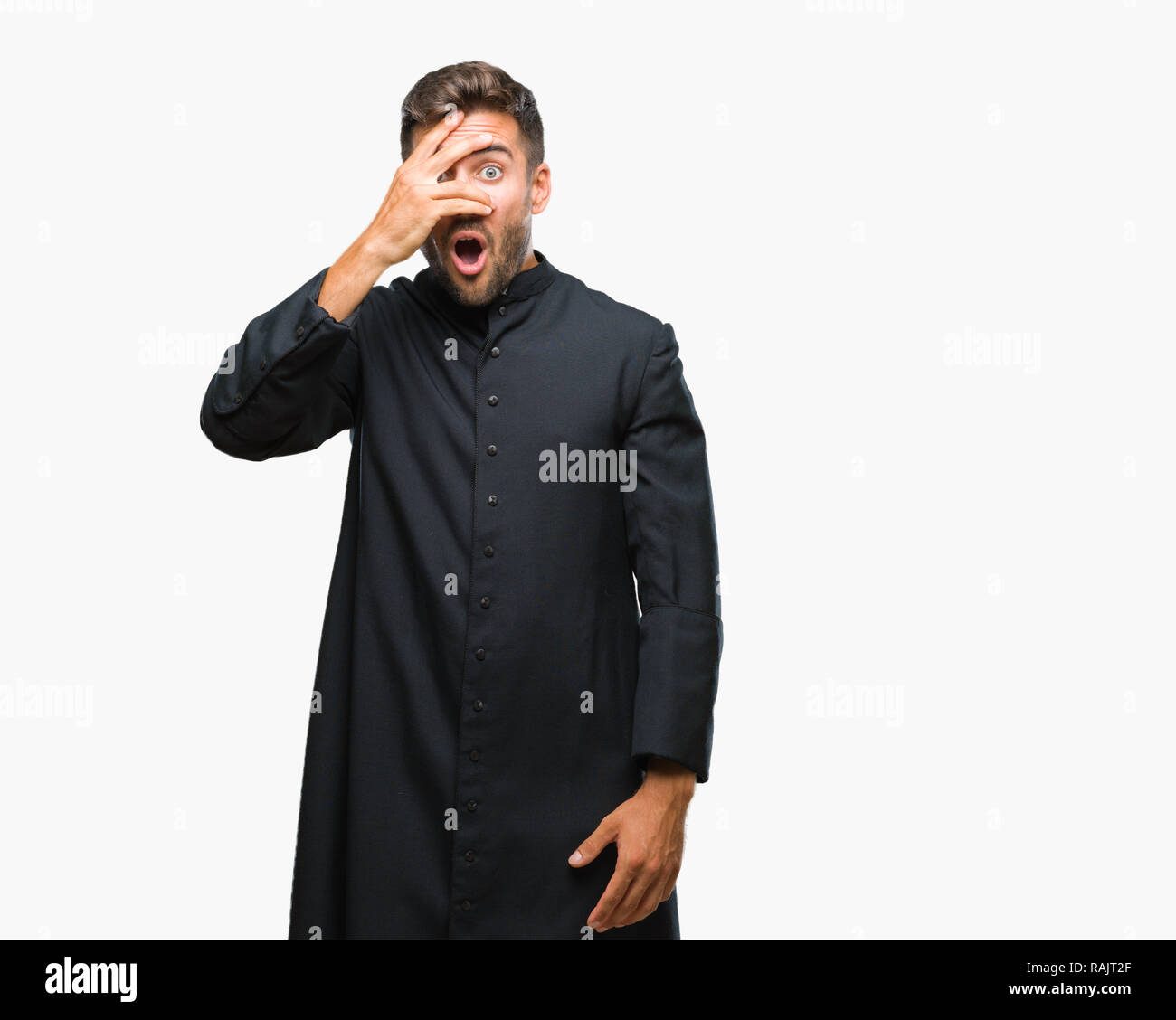 Young catholic christian priest man over isolated background peeking in ...