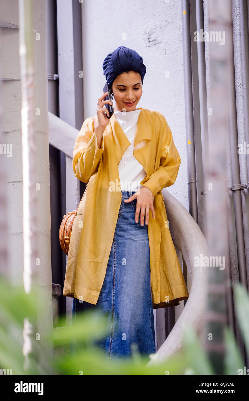 A young and beautiful Muslim Asian woman is talking on her smartphone ...
