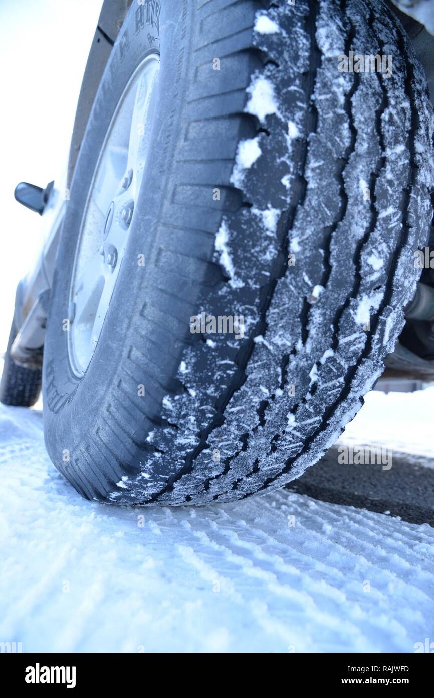 An icy vehicle tire is shown on top of a layer of ice during the winter ...