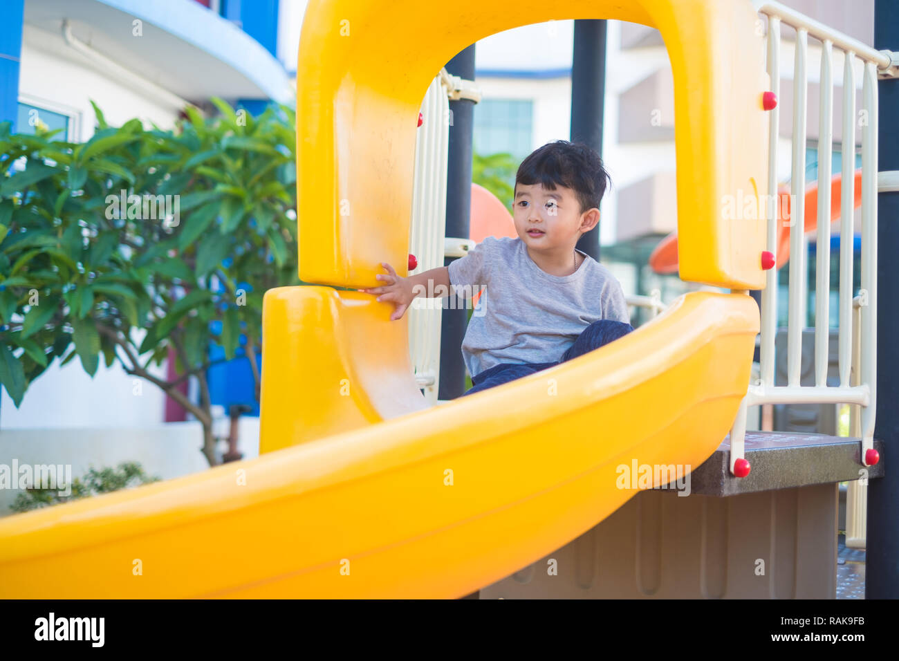 Asian kid playing slide at the playground under the sunlight in summer ...