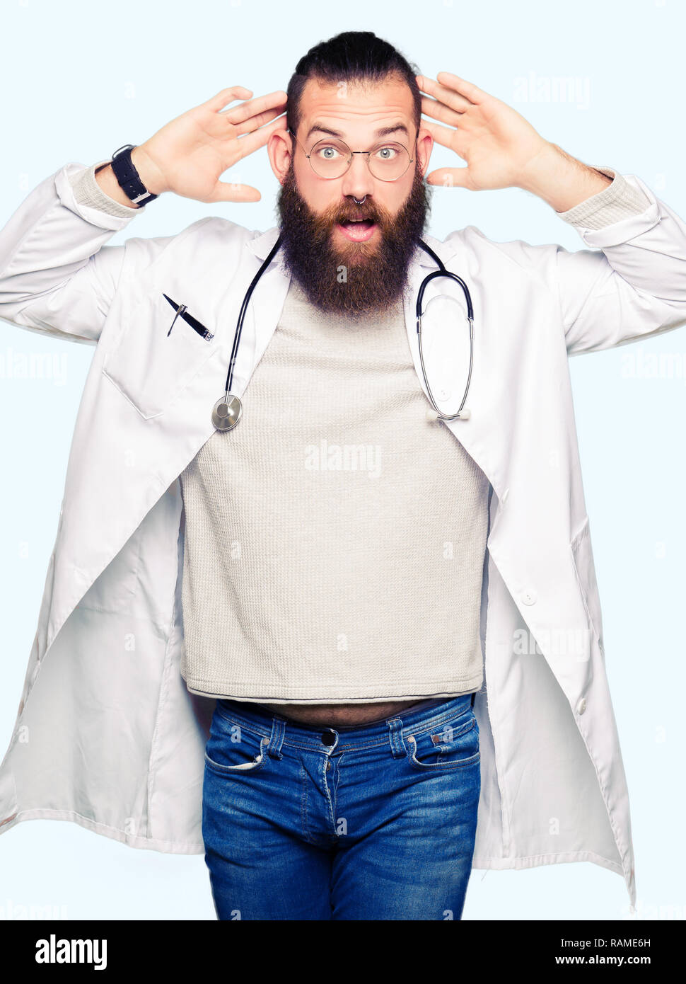 Young blond doctor man with beard wearing medical coat Crazy and scared ...