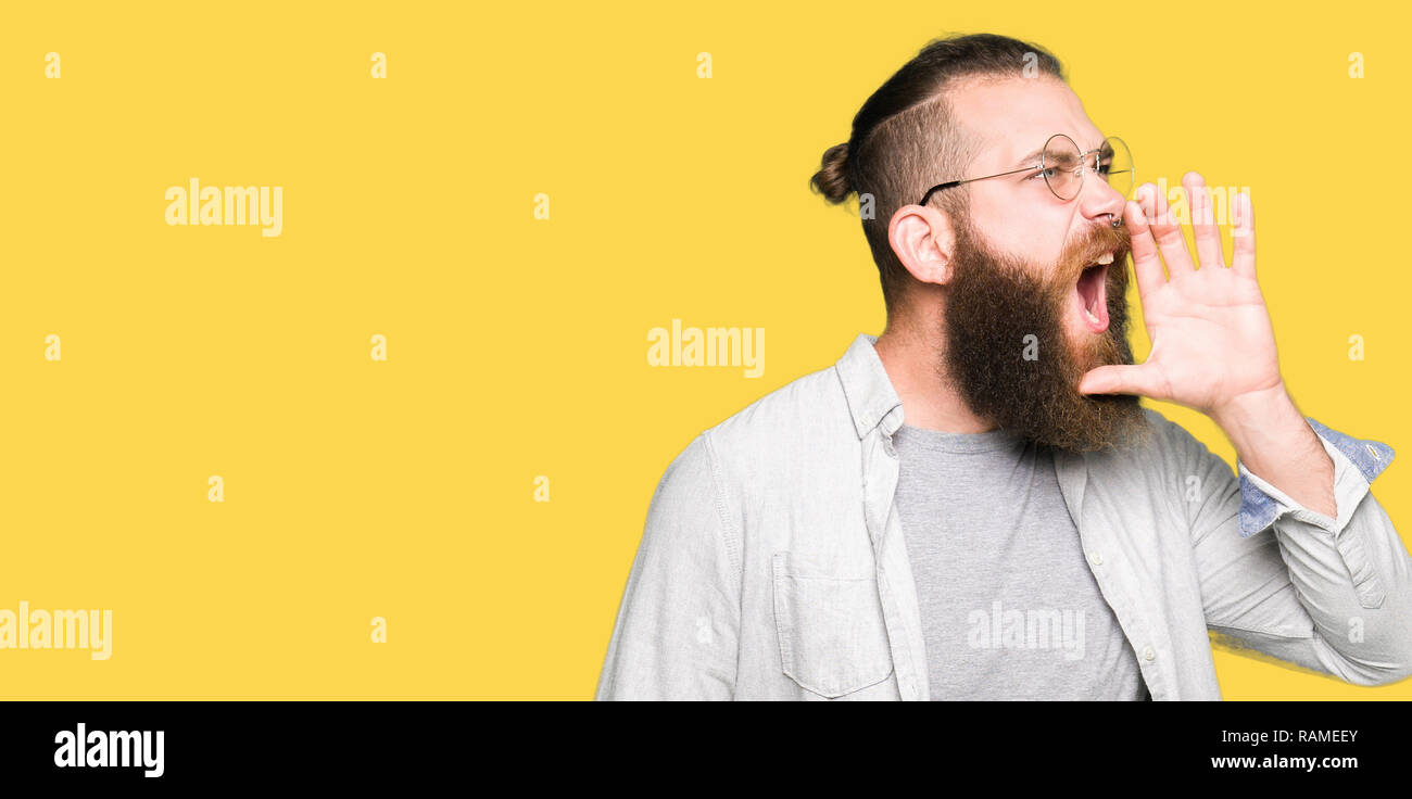 Young blond man wearing glasses shouting and screaming loud to side ...