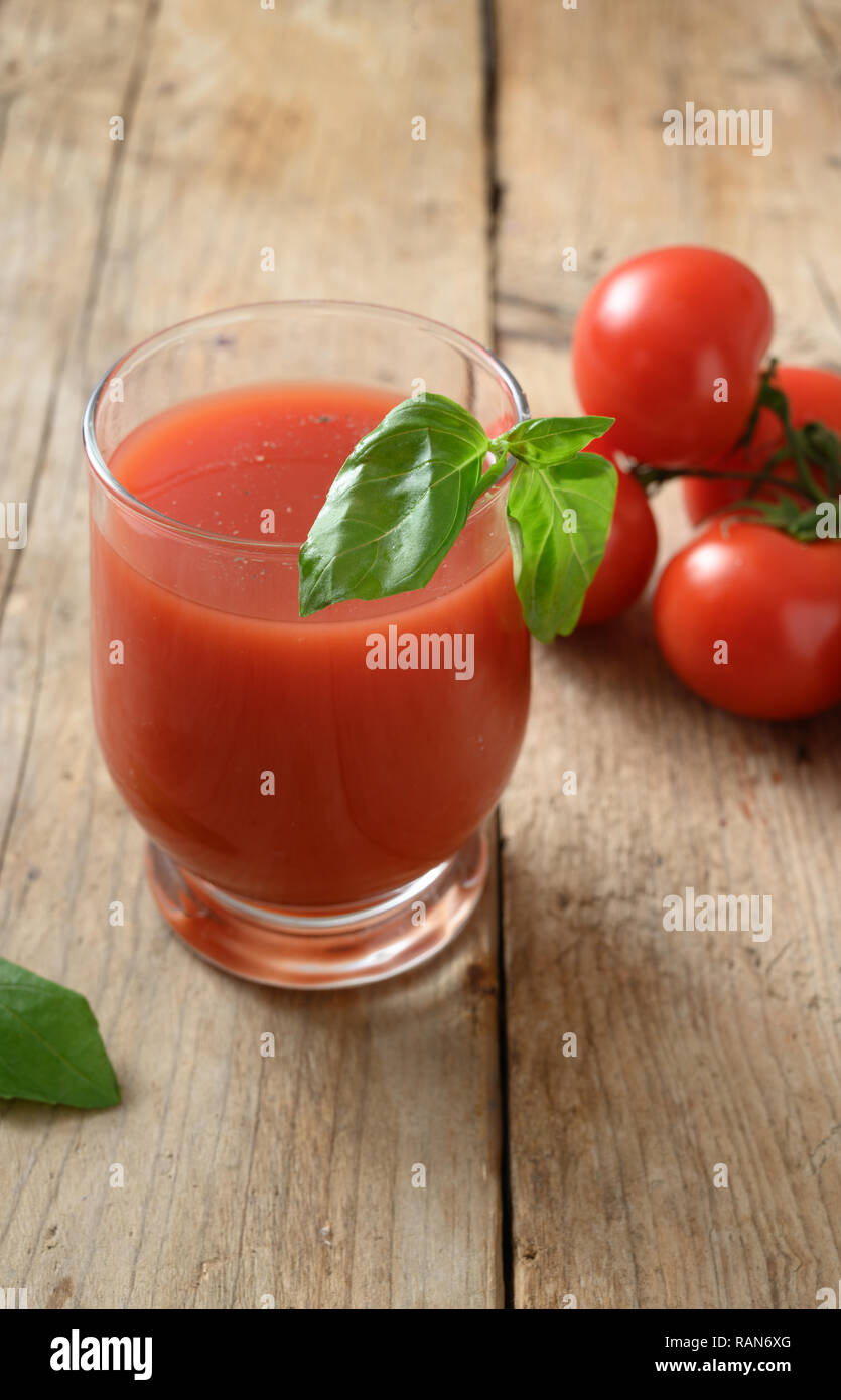 fresh tomato juice in a drinking glass with basil garnish on a rustic ...