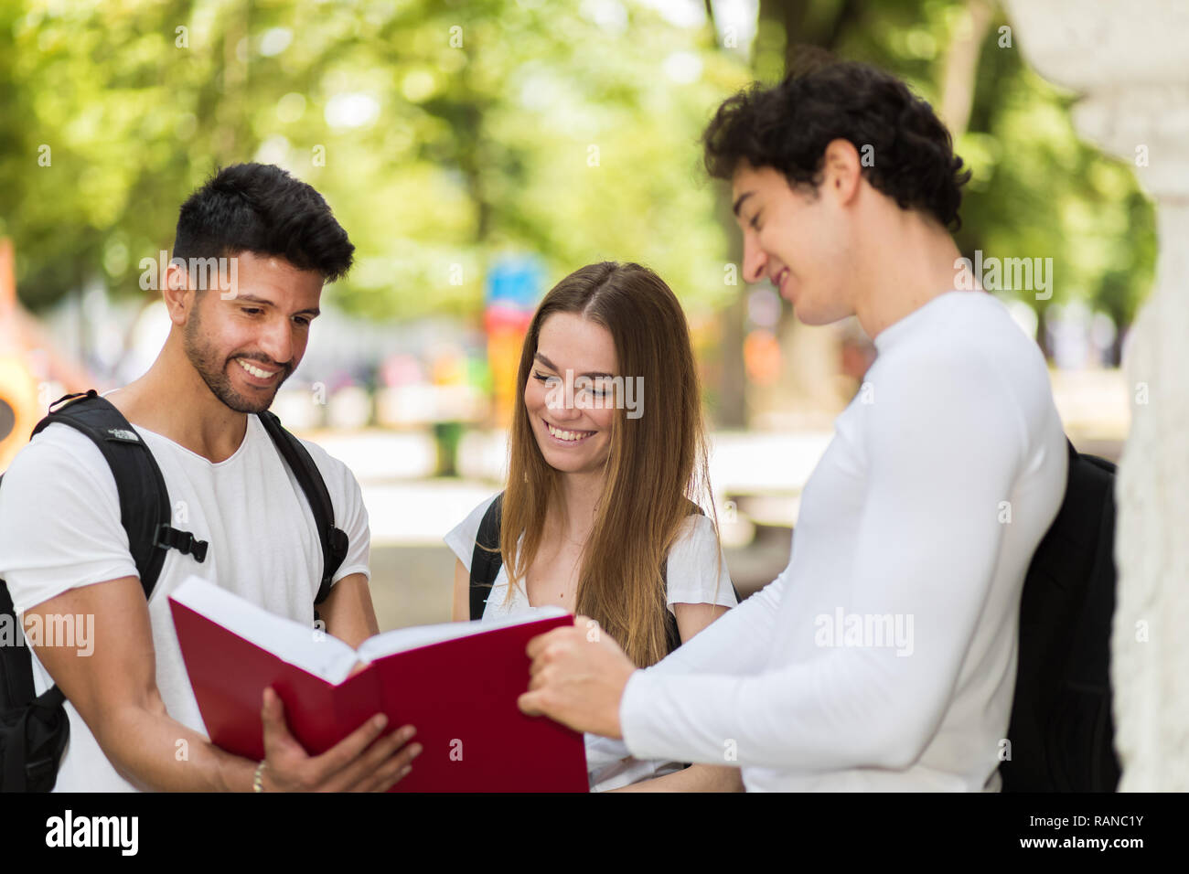 Three students talking to each other outdoor in a college courtyard ...