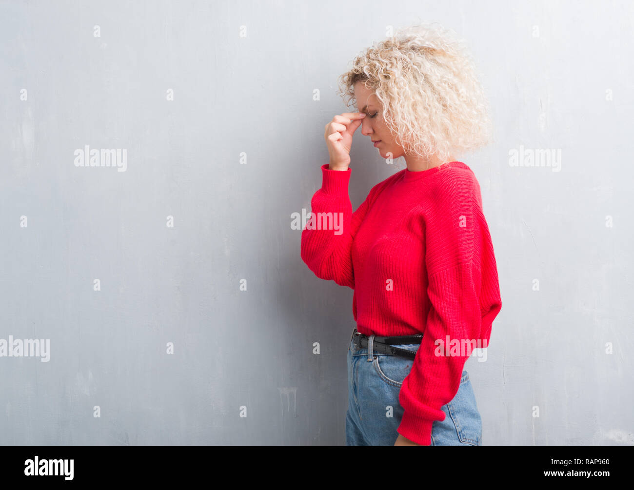 Young blonde woman with curly hair over grunge grey background tired ...