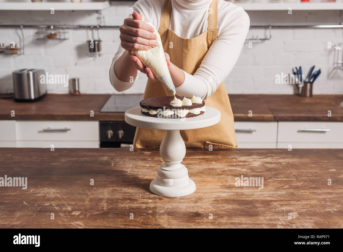 mid section of woman in apron decorating gourmet sweet cake with cream ...