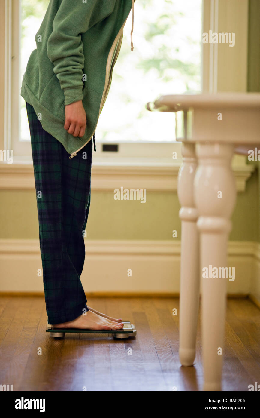 Woman stands on a set of scales and leans forward to look at the total ...