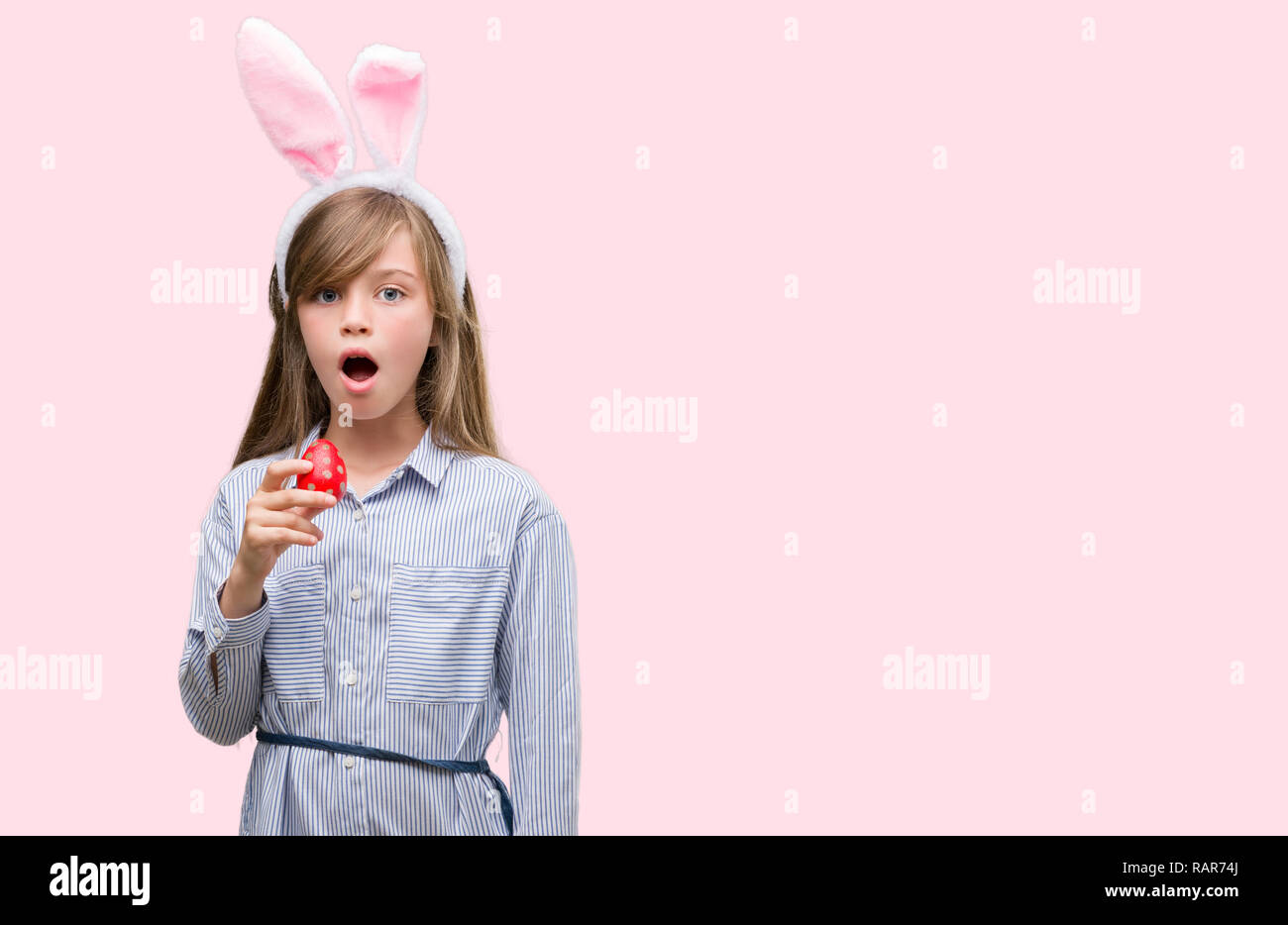 Young blonde child wearing easter bunny ears scared in shock with a ...