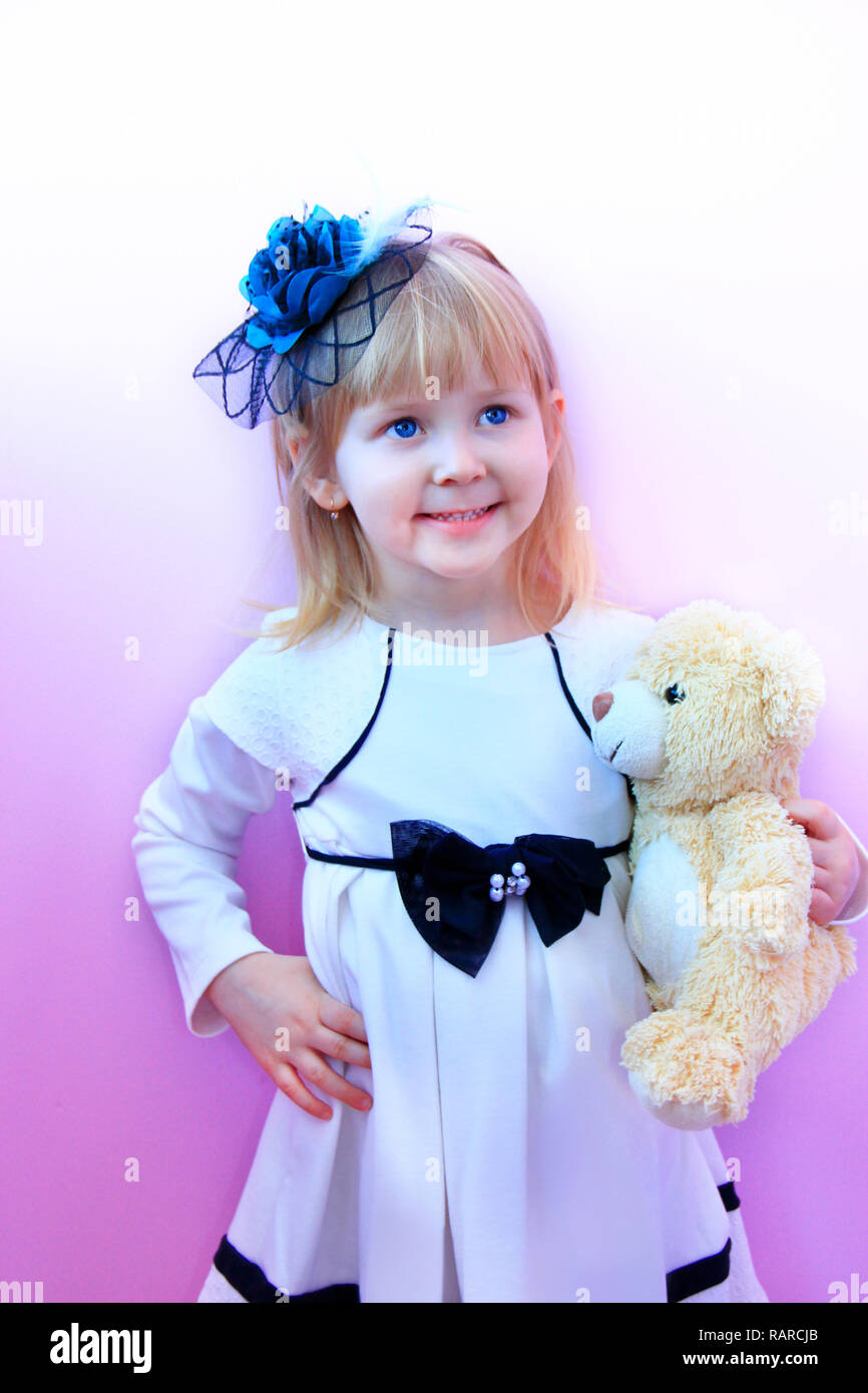 Little girl in fashionable hat and with toy bear cub in hands smiling ...
