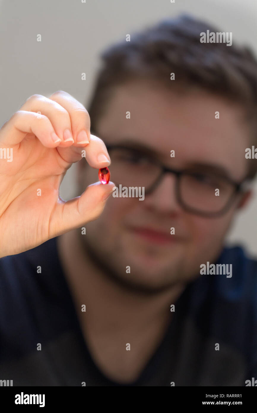 A teenage boy holding a red pill or drug in his hand before taking the ...