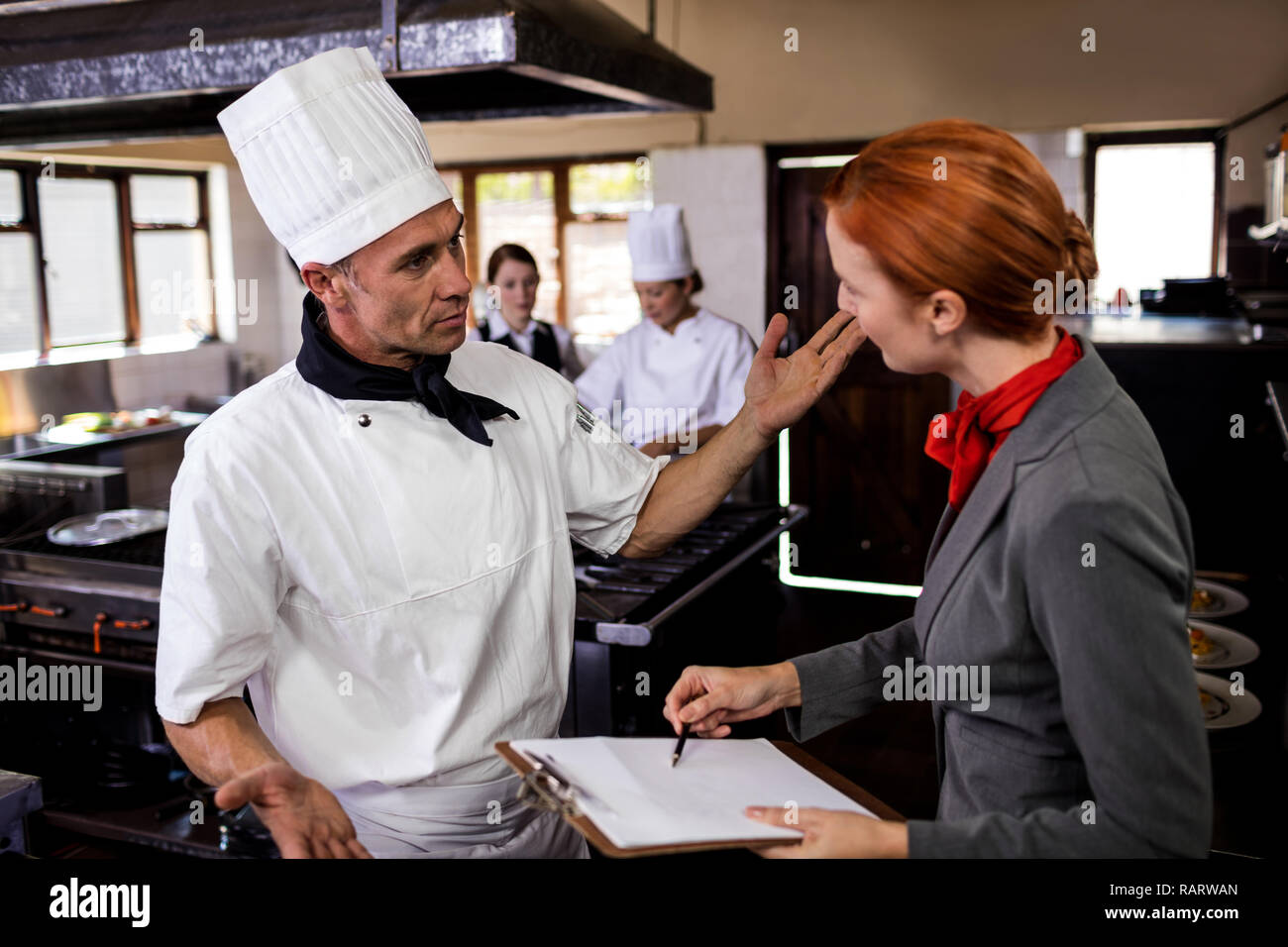 Female manager and male chef interacting with each other in kitchen ...