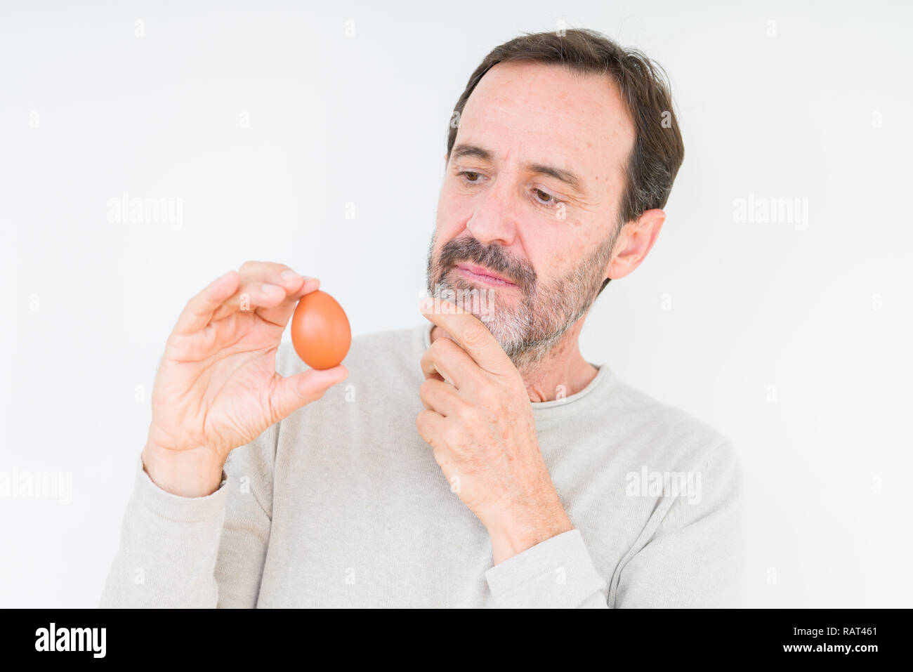 Senior man holding fresh egg over isolated background serious face ...