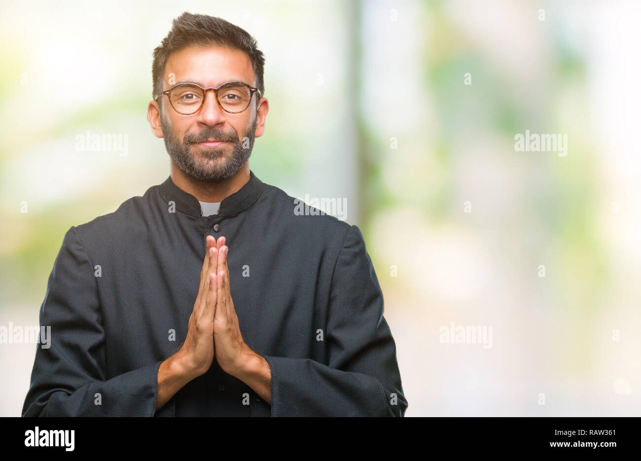 Adult hispanic catholic priest man over isolated background praying ...