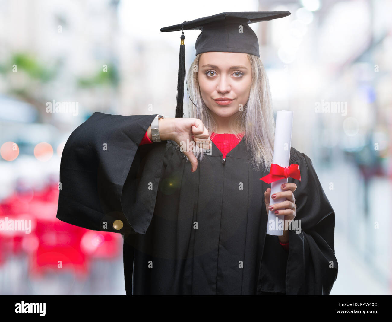 Young blonde woman wearing graduate uniform holding degree over ...