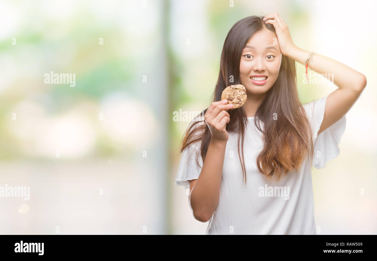 Young asian woman eating chocolate chip cookie over isolated background ...
