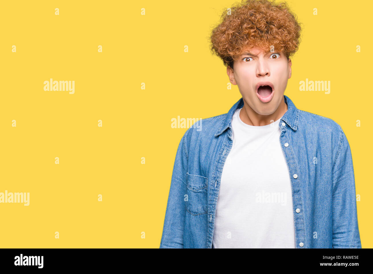 Young handsome man with afro hair wearing denim jacket In shock face ...