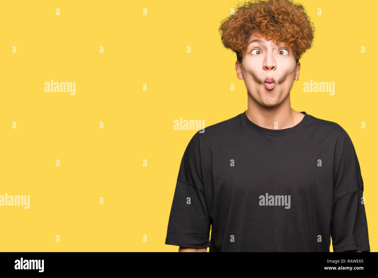 Young handsome man with afro hair wearing black t-shirt making fish ...