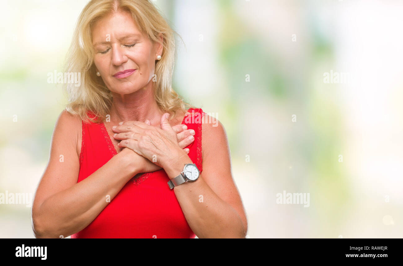 Middle age blonde woman over isolated background smiling with hands on chest with closed eyes ...