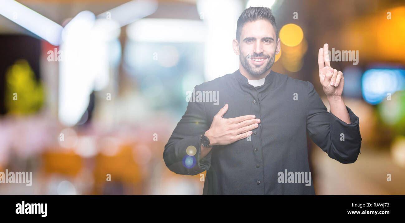 Young Christian priest over isolated background Swearing with hand on ...